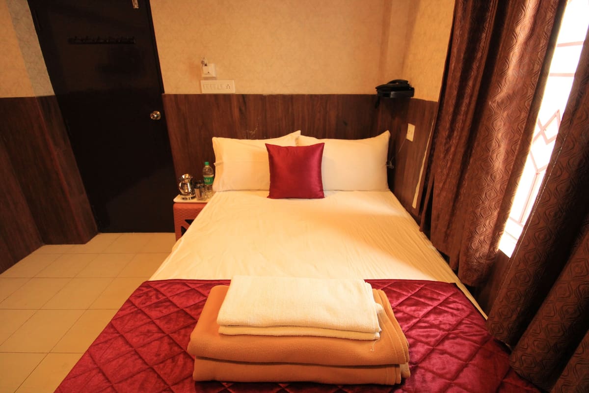 Quarto de hotel com uma cama, mesa de cabeceira, garrafa de água e travesseiro vermelho.