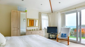 Quarto com cama grande, televisão, cadeira, cômoda e porta de vidro corrediça para uma varanda.