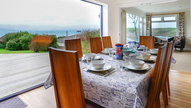 Uma sala de jantar com mesa posta para seis, com vista para o mar.