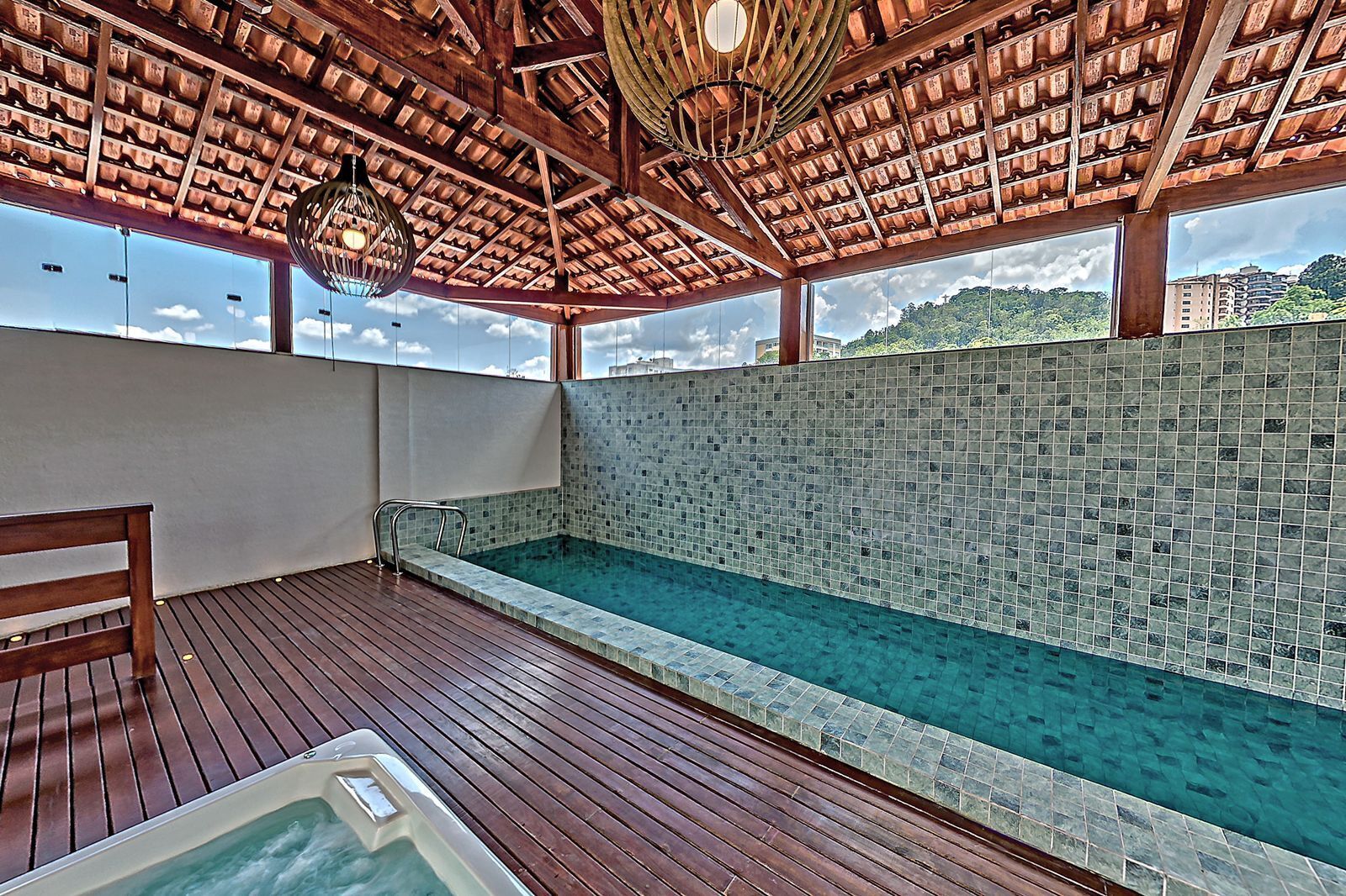Piscina no terraço com deck de madeira, área de estar e parede revestida com azulejos.