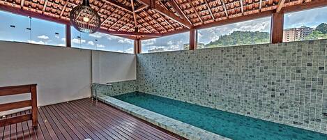 Piscina no terraço com deck de madeira, área de estar e parede revestida com azulejos.