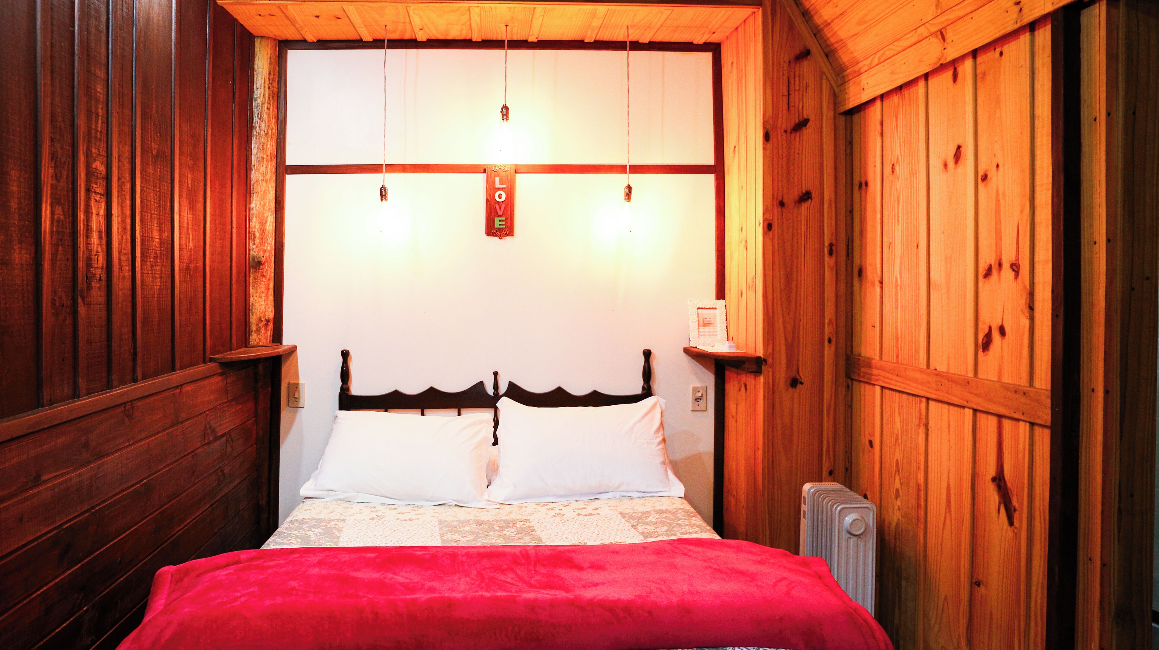 Quarto de madeira com cama, radiador e teto de madeira.