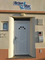 Uma porta branca com um arco decorativo, uma pequena janela acima e uma placa acima da porta com a inscrição "Brisa do Mar" e informações de contato.
