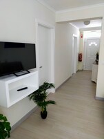 Corredor com televisão de tela plana na parede, um vaso de planta e um extintor de incêndio também na parede.
