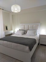 Quarto bem organizado com uma cama grande, mesas de cabeceira, luminária pendente e um vaso com planta.