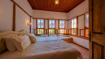 Quarto com cama grande, um banco e várias janelas com cortinas.
