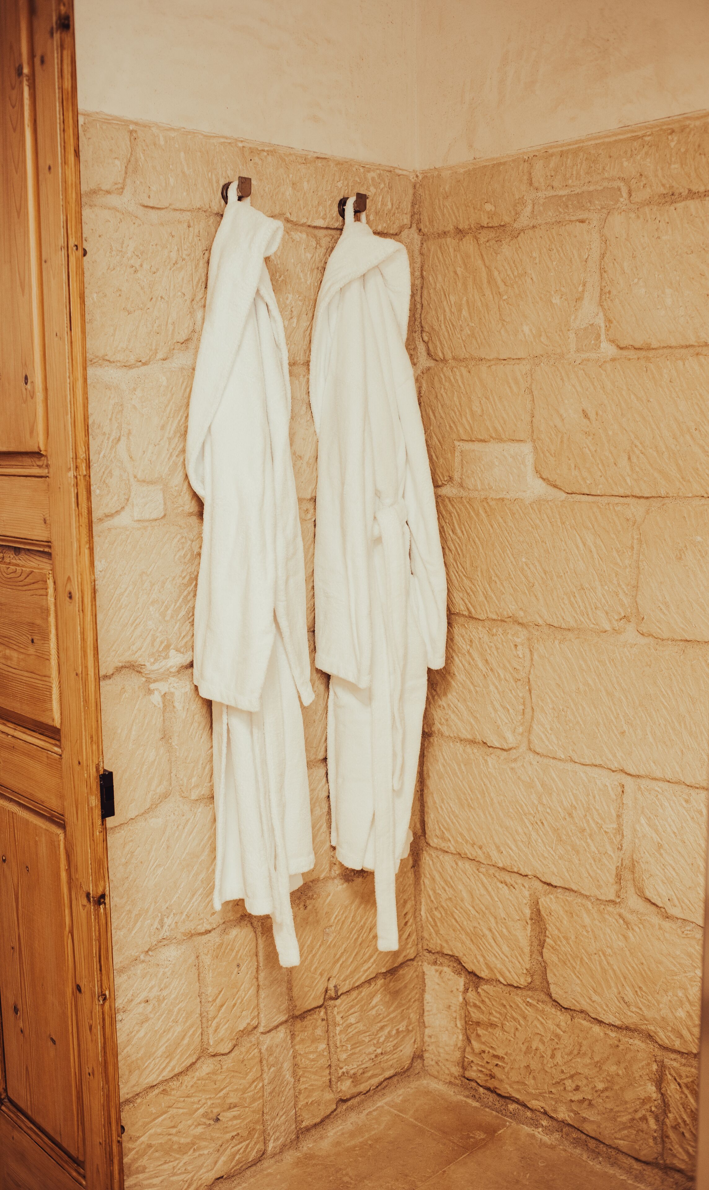 Uma parede de pedra com dois robes brancos pendurados em ganchos.