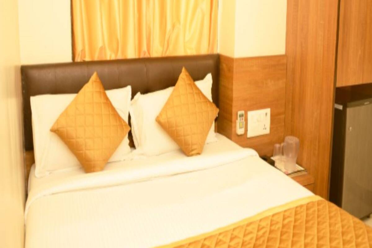 Cama com cobertura acolchoada, duas almofadas, mesa de cabeceira com telefone e guarda-roupa de madeira.