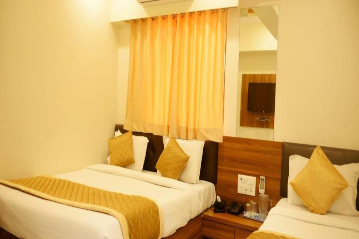 Quarto de hotel com duas camas, cabeceira de madeira, mesa de cabeceira, espelho e aparelho de ar condicionado.