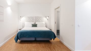 Quarto com cama, paredes brancas, cabeceira estampada e piso de madeira.