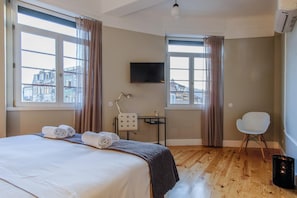 Quarto de hotel com cama, escrivaninha, cadeira e televisão.