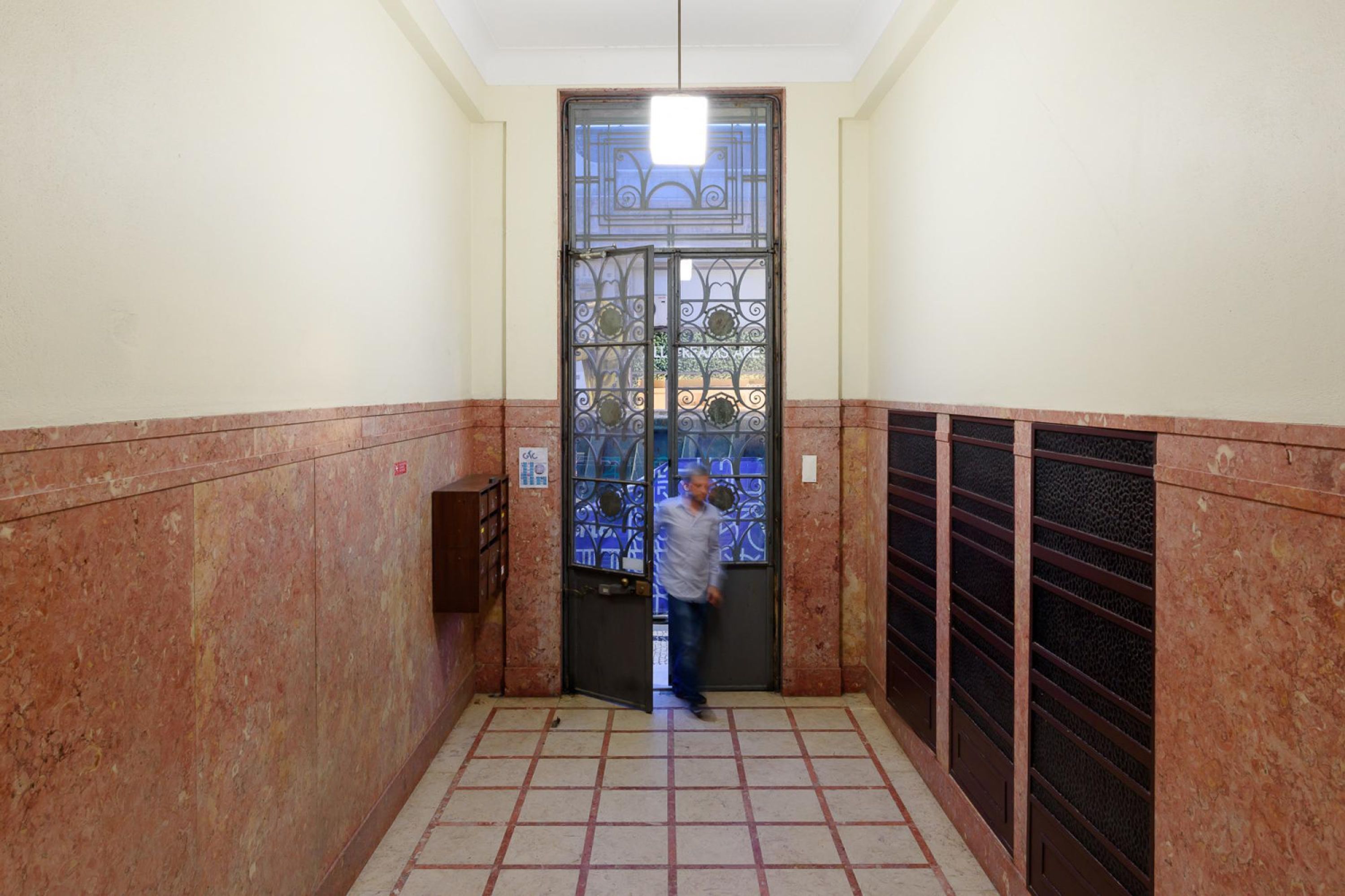 Um corredor com piso de azulejos e uma porta com grade de metal.