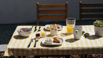 Mesa posta com itens de café da manhã, incluindo croissants, uma tigela de frutas vermelhas, um copo de suco de laranja e um jarro de leite.