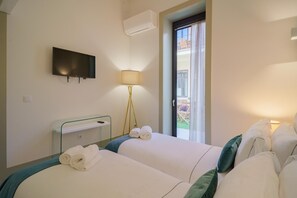 Quarto de hotel com duas camas, televisão, abajur e vista para o exterior.