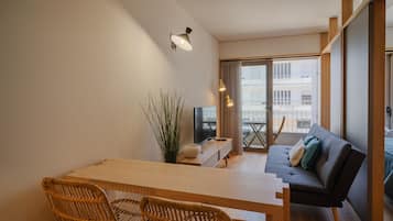 Uma sala de estar moderna com uma mesa de jantar de madeira, duas cadeiras de vime, um sofá cinza e uma grande janela com vista para a cidade.