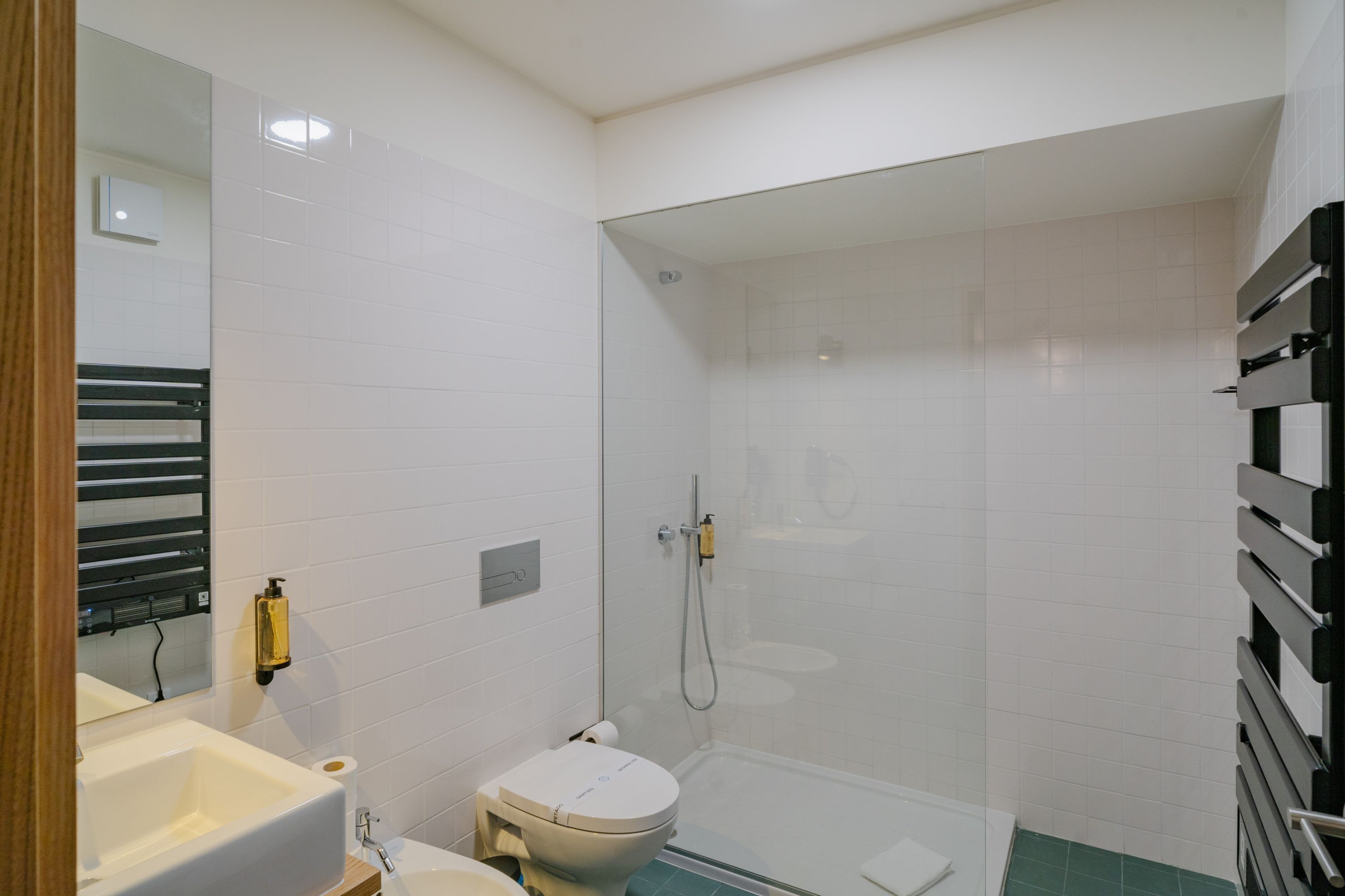 Uma casa de banho moderna com cabine de duche em vidro, sanita branca e lavatório com espelho.