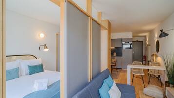 Quarto de hotel moderno com cama, sofá, área de refeições e cozinha compacta.