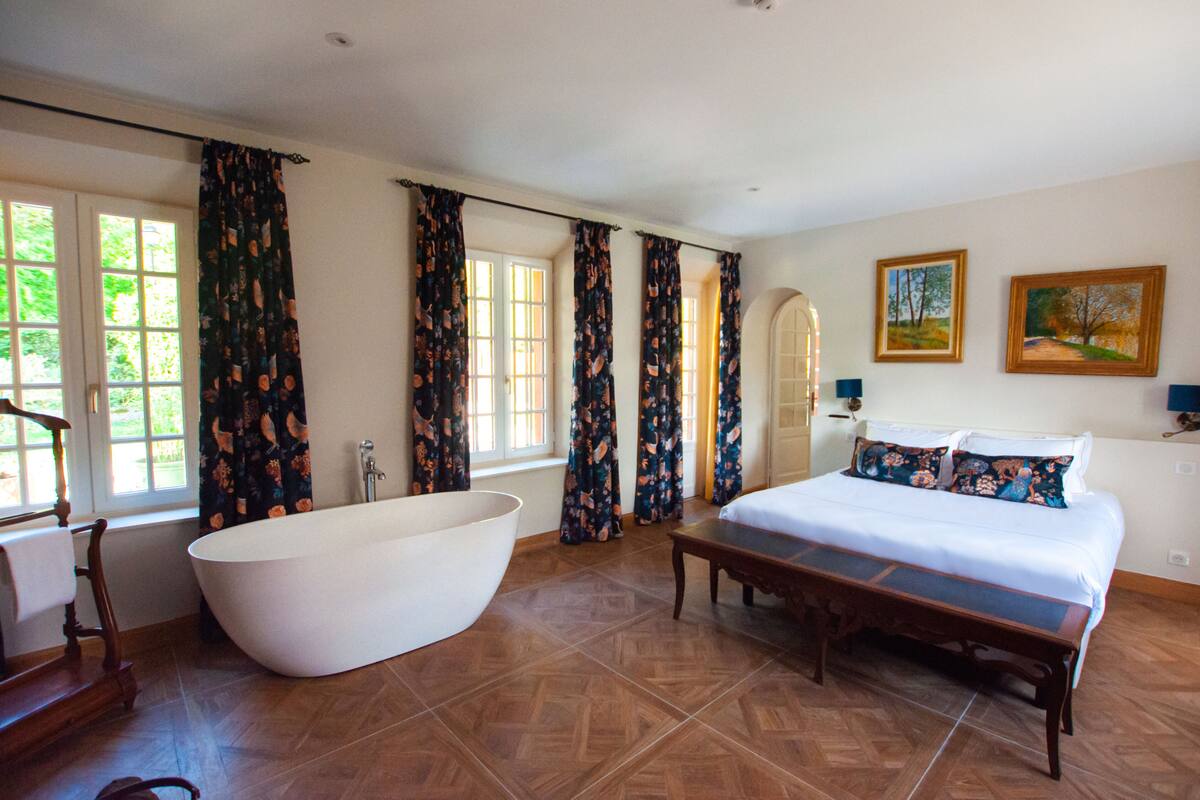 Um quarto espaçoso com uma cama grande, uma banheira e um banco de madeira.