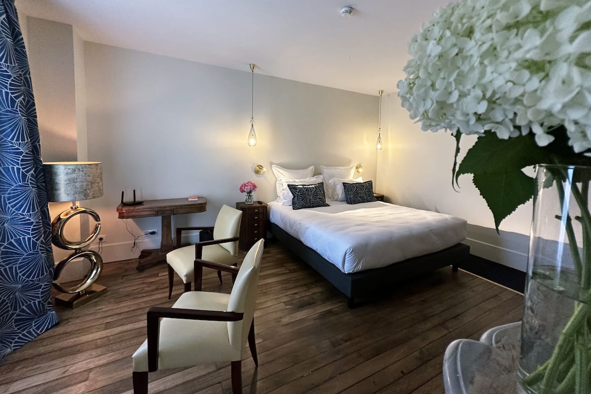 Quarto de hotel com cama, escrivaninha, cadeira e um vaso com flores.