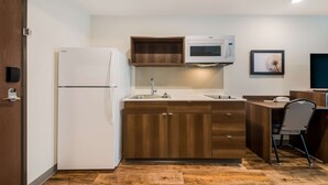 Cozinha compacta com geladeira, micro-ondas, pia e armários de madeira.