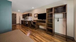 Quarto moderno e bem iluminado com piso de madeira, escrivaninha com computador, televisão e estantes embutidas com cestos.