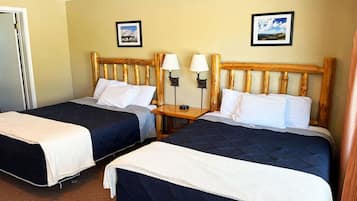 Quarto de hotel com duas camas, cada uma com cabeceira de madeira, roupa de cama branca e mesa de cabeceira com luminária.