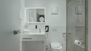 Uma casa de banho moderna com cabine de duche em vidro, lavatório branco com espelho e sanita.