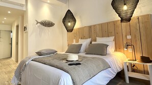 Quarto moderno com teto de madeira, uma cama grande com roupa de cama branca e duas luminárias pendentes.