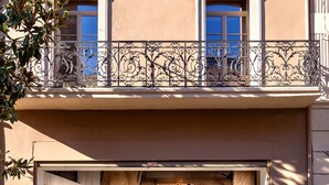 Um edifício com espaço comercial no andar térreo, incluindo área de refeições com mesas e cadeiras, e varanda com grades de metal decoradas.