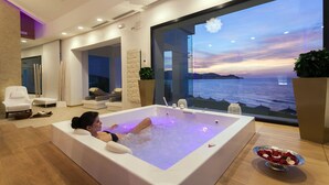 Um spa moderno com uma banheira grande, vista para o mar e uma área de estar com cadeiras e mesa de massagem.