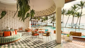 Uma área à beira da piscina com um conjunto de assentos circulares, piscina e palmeiras ao fundo.