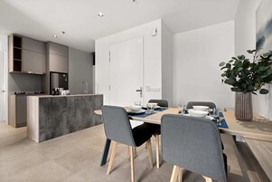 Cozinha moderna com armários cinzentos, ilha integrada e área de refeições com mesa posta para dois.