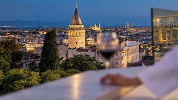 Paisagem urbana com uma torre imponente e uma mesa de vidro com uma taça de vinho.