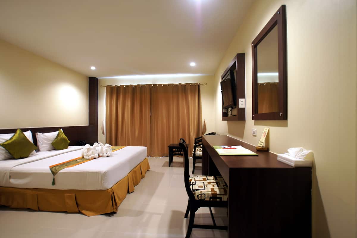 Quarto de hotel com cama, escrivaninha, cadeiras e televisão.