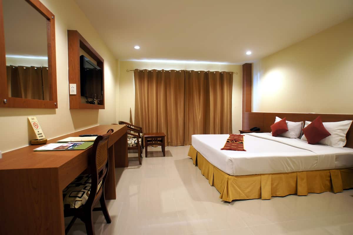 Quarto de hotel com cama, escrivaninha, cadeira e televisão.