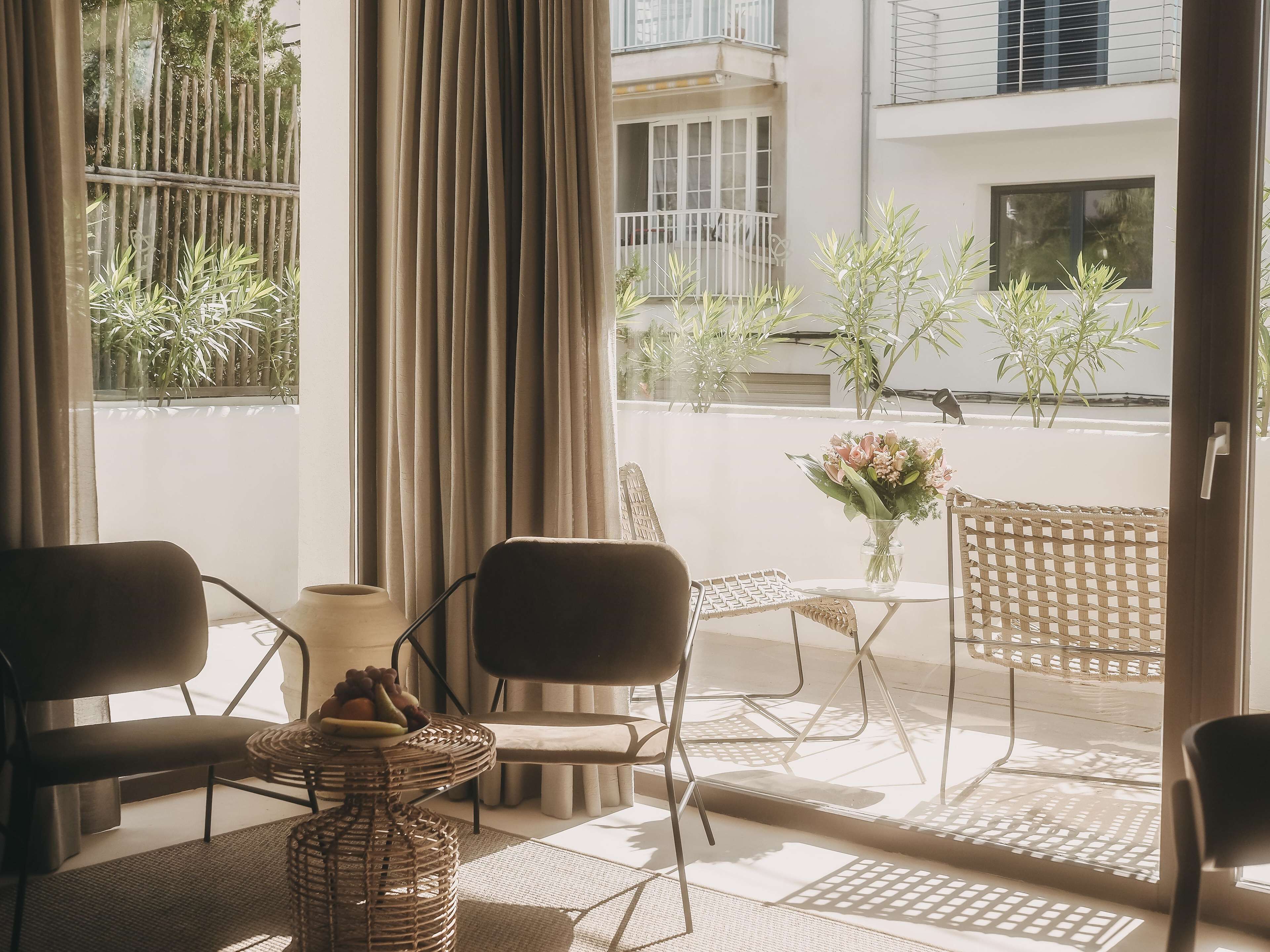 Uma varanda com mobiliário de vime, uma mesa pequena com um vaso de flores e vista para uma área residencial.