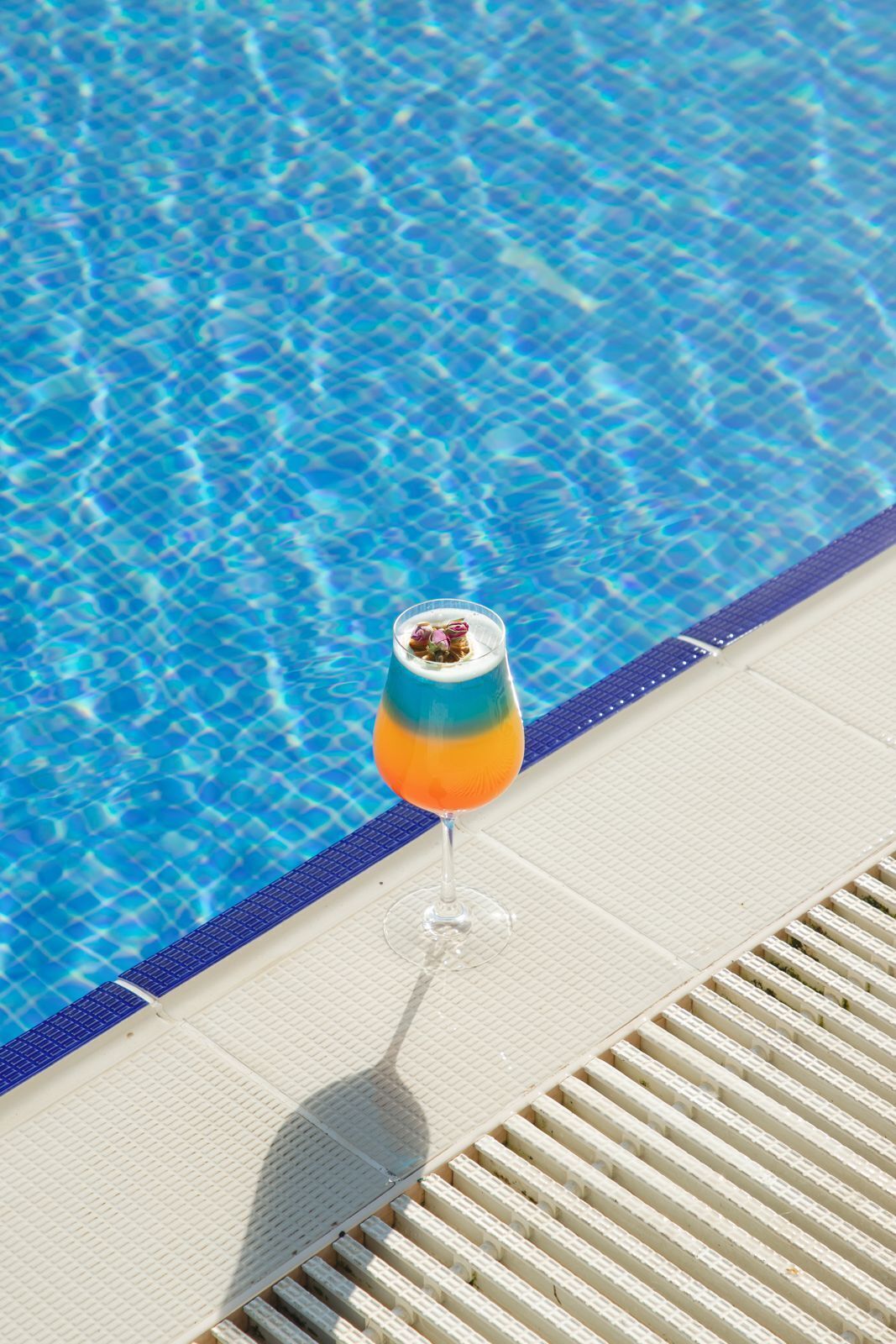 Um copo de cocktail com um design em camadas ao lado de uma piscina.