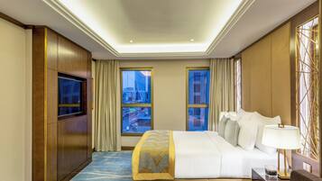Quarto de hotel com uma cama, televisão, escrivaninha com abajur e duas janelas com cortinas.