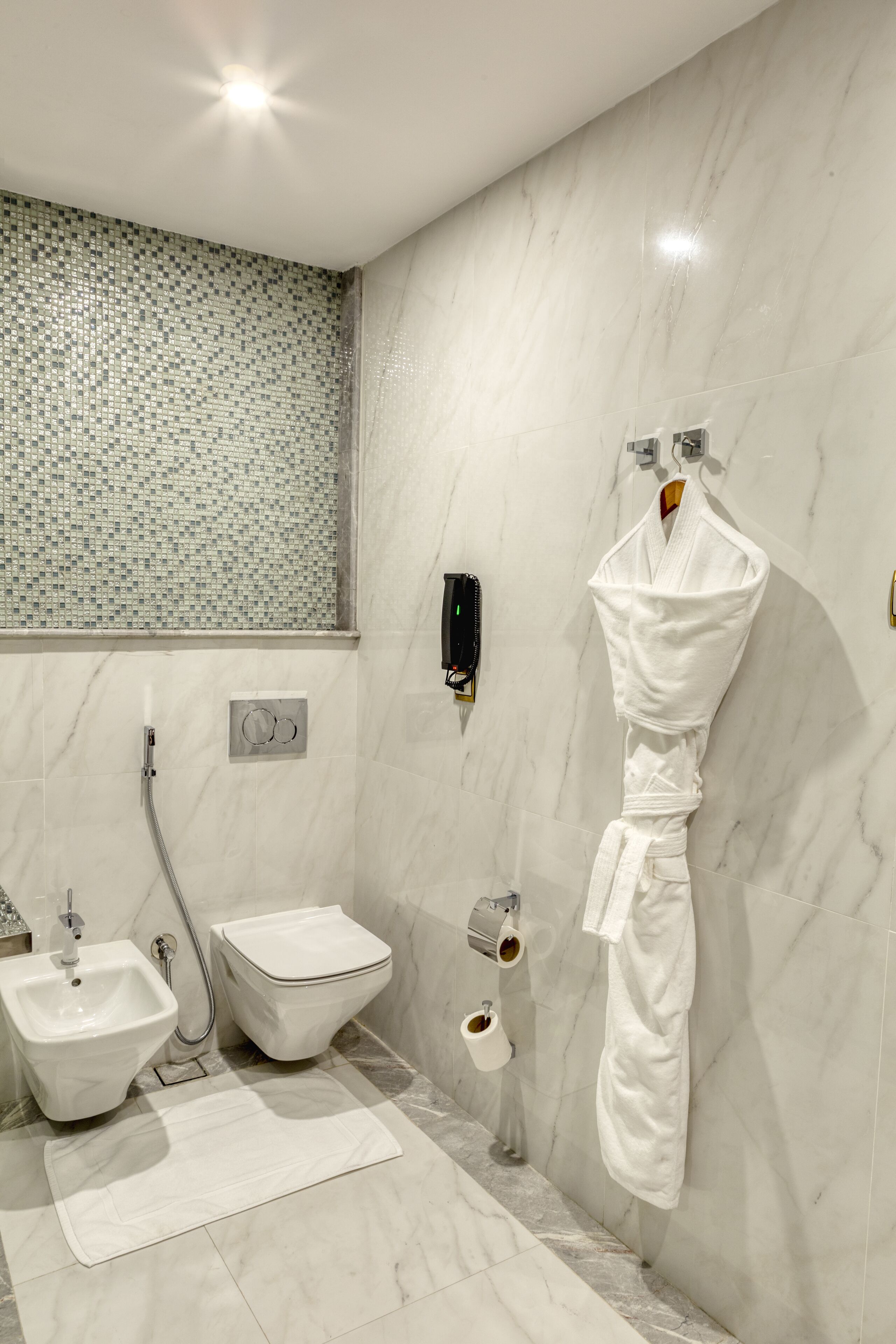 Uma casa de banho moderna com bidé, sanita e um roupeiro pendurado na parede.
