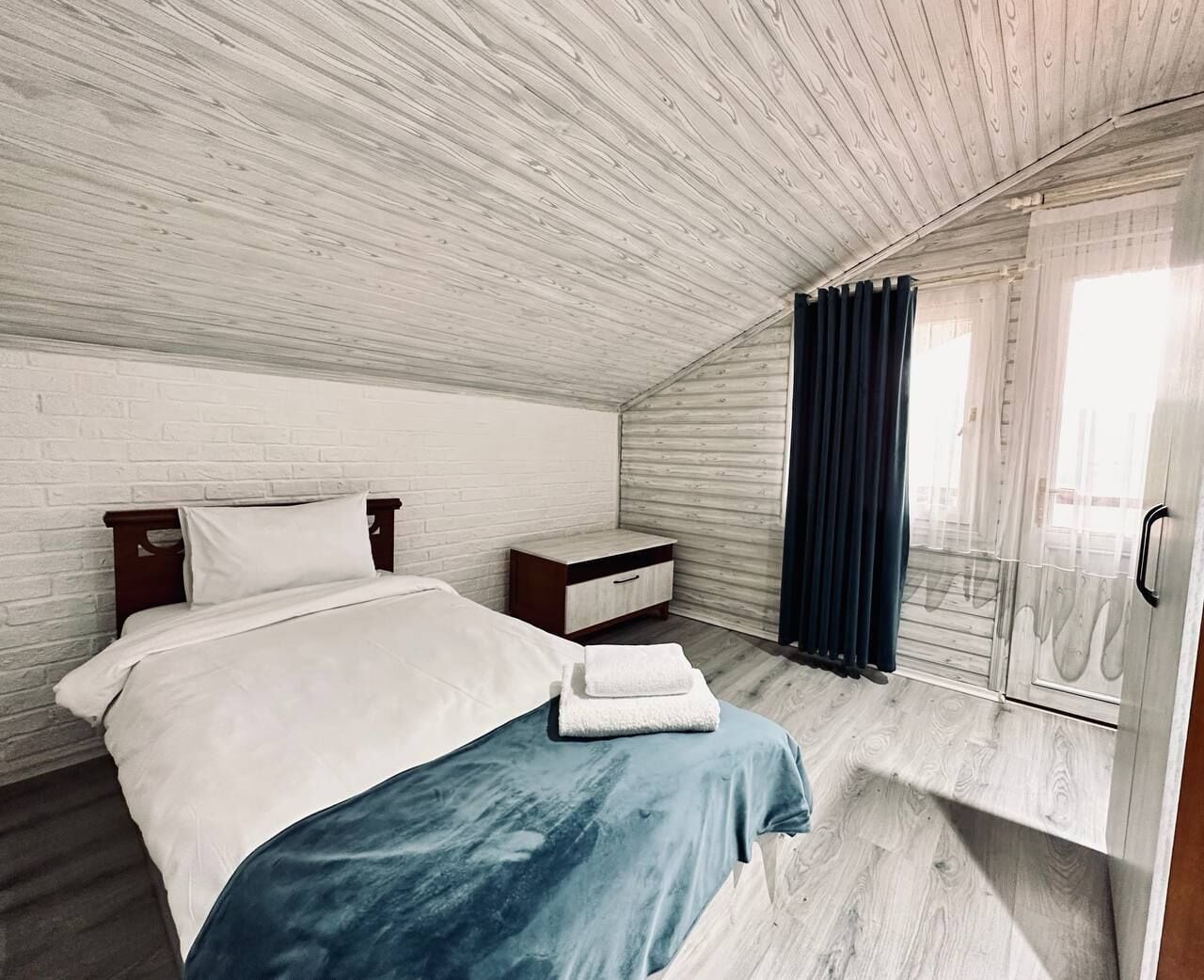 Um quarto com uma cama, uma mesa de cabeceira, uma janela com cortinas e teto de madeira.