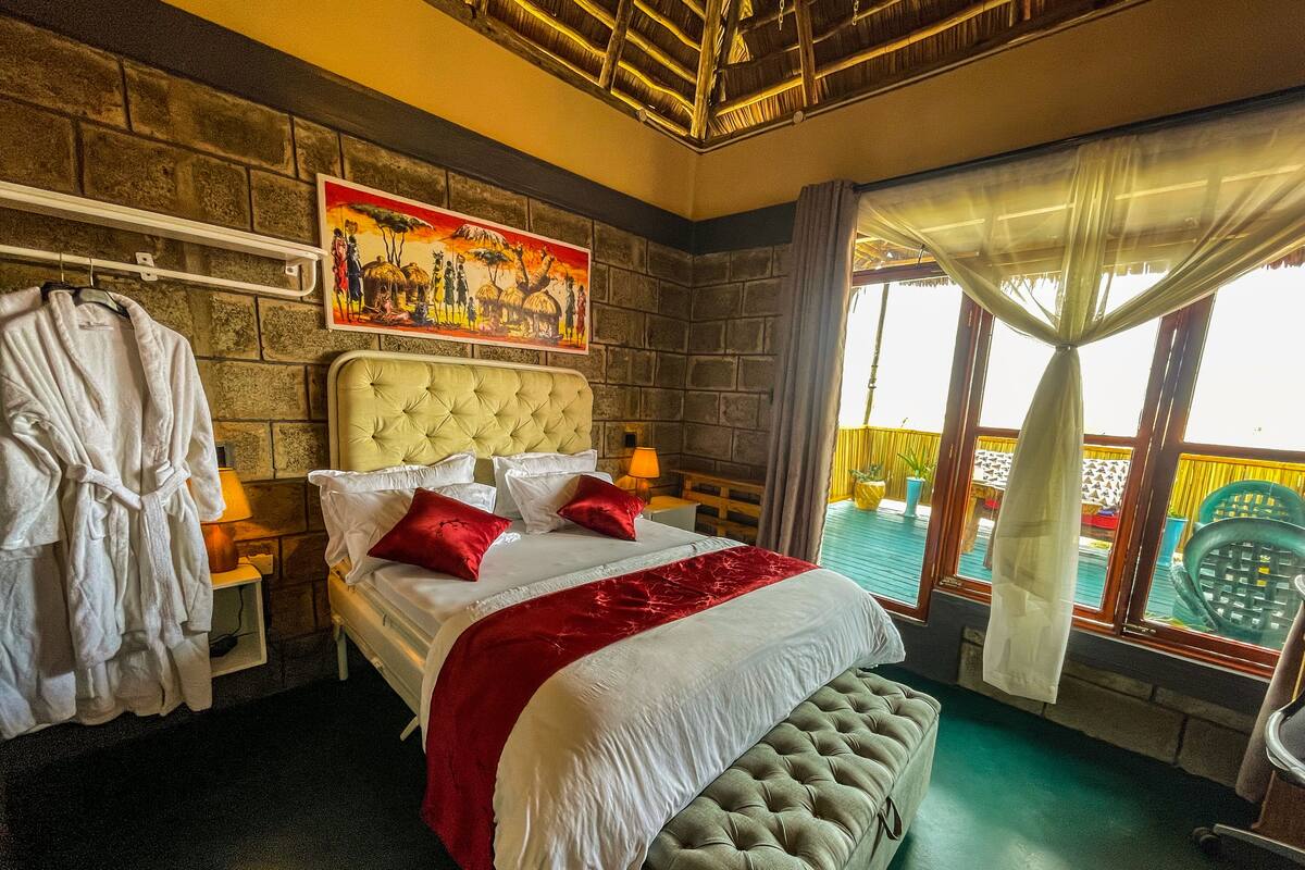 Quarto com uma cama grande, um banquinho, um cabideiro e um quadro na parede.