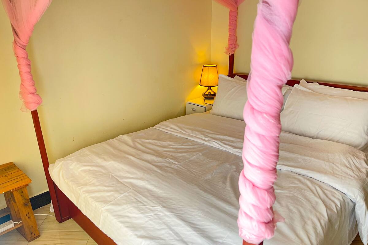 Uma cama com dossel, uma mesinha de cabeceira e uma luminária.