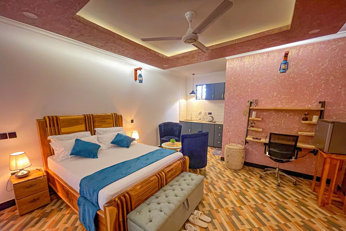 Quarto com cama de madeira, um banco, chinelos, escrivaninha e uma cadeira.