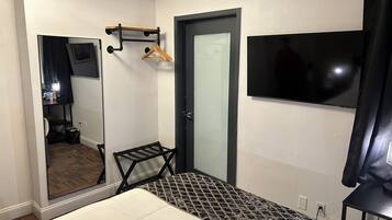 Quarto de hotel com cama, televisão na parede, espelho e um pequeno espaço de estar com um banco.