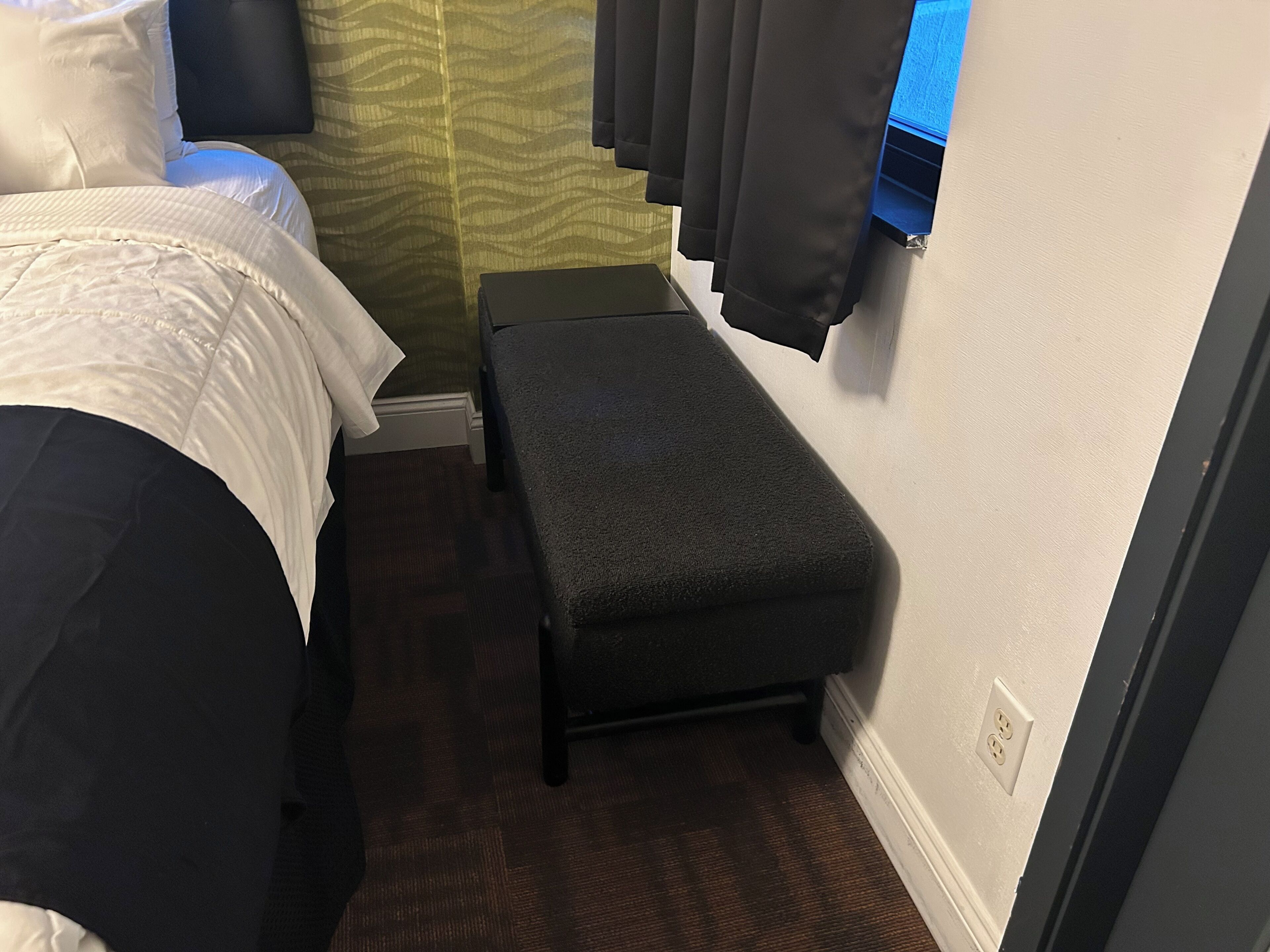 Quarto de hotel com cama, um banco, televisão na parede e janela com cortinas.