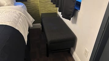 Quarto de hotel com cama, um banco, televisão na parede e janela com cortinas.