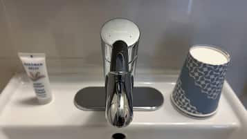 Uma pia de banheiro com uma torneira cromada, um tubo de loção corporal e uma xícara estampada.
