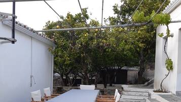 Pátio externo com mesa e cadeiras, cercado por piso de pedra e vegetação.