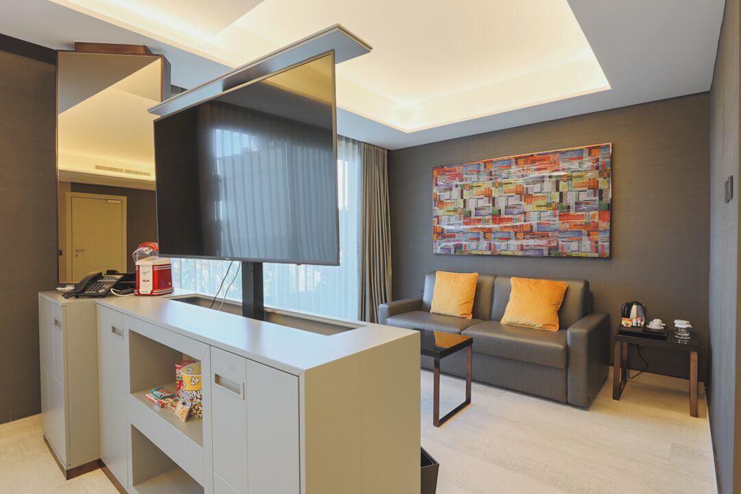 Quarto de hotel moderno com escrivaninha, sofá, mesa de centro e uma grande pintura abstrata na parede.