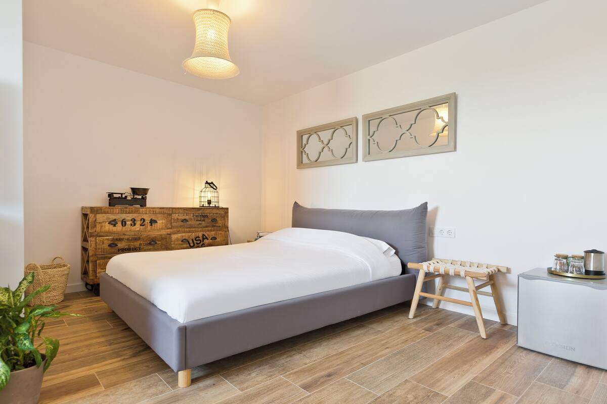 Quarto moderno com cama, cómoda de madeira, mesa de cabeceira e decoração na parede.